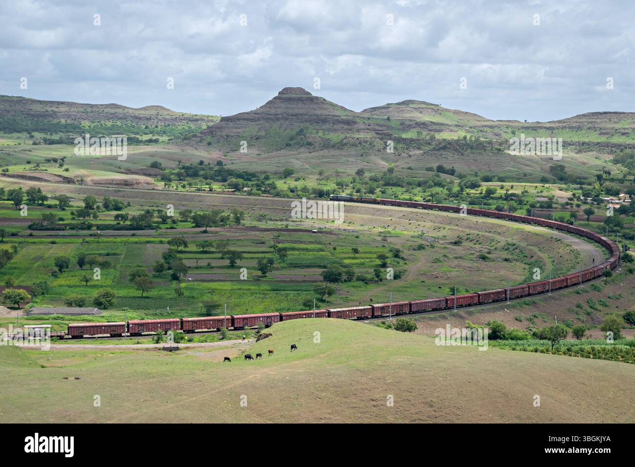 Long goods freight train passing through a big curve in hilly railway ...