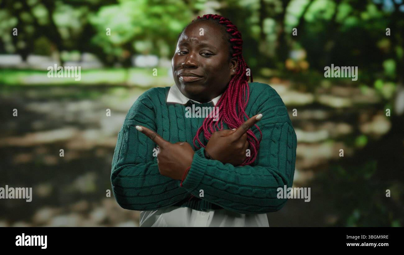 Woman with pink braids wearing green sweater points in opposite ...
