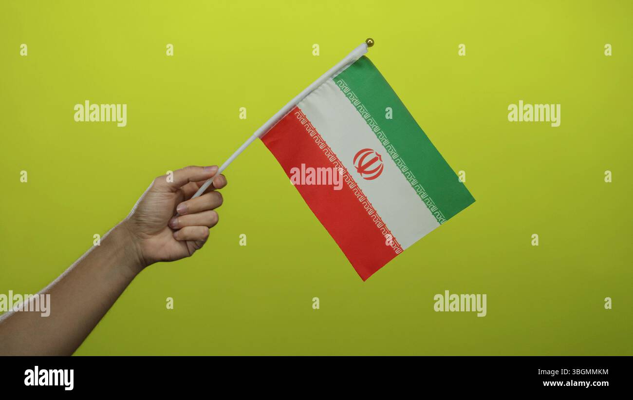 Hand holding iranian flag against vibrant yellow wall shows national ...