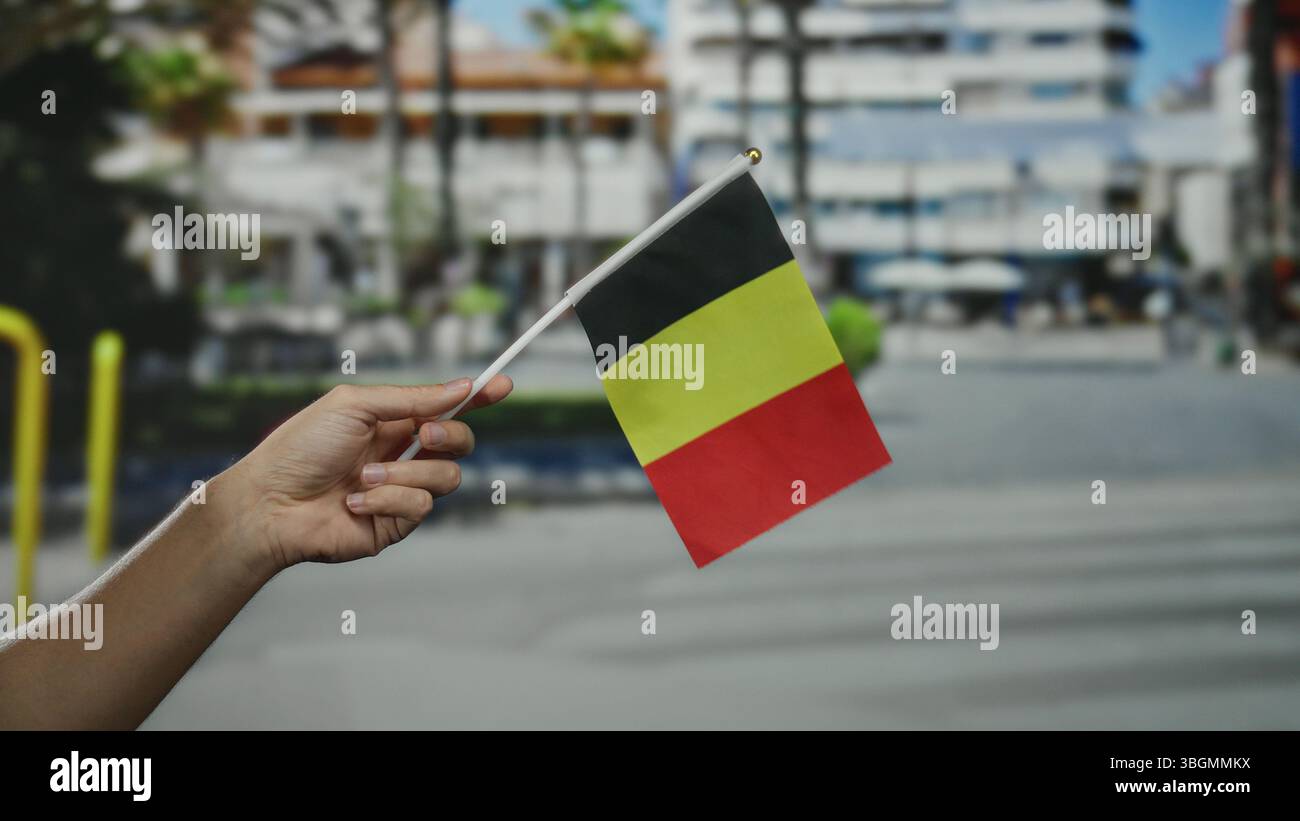 Hand holds belgian flag in outdoor city street setting, signifying ...