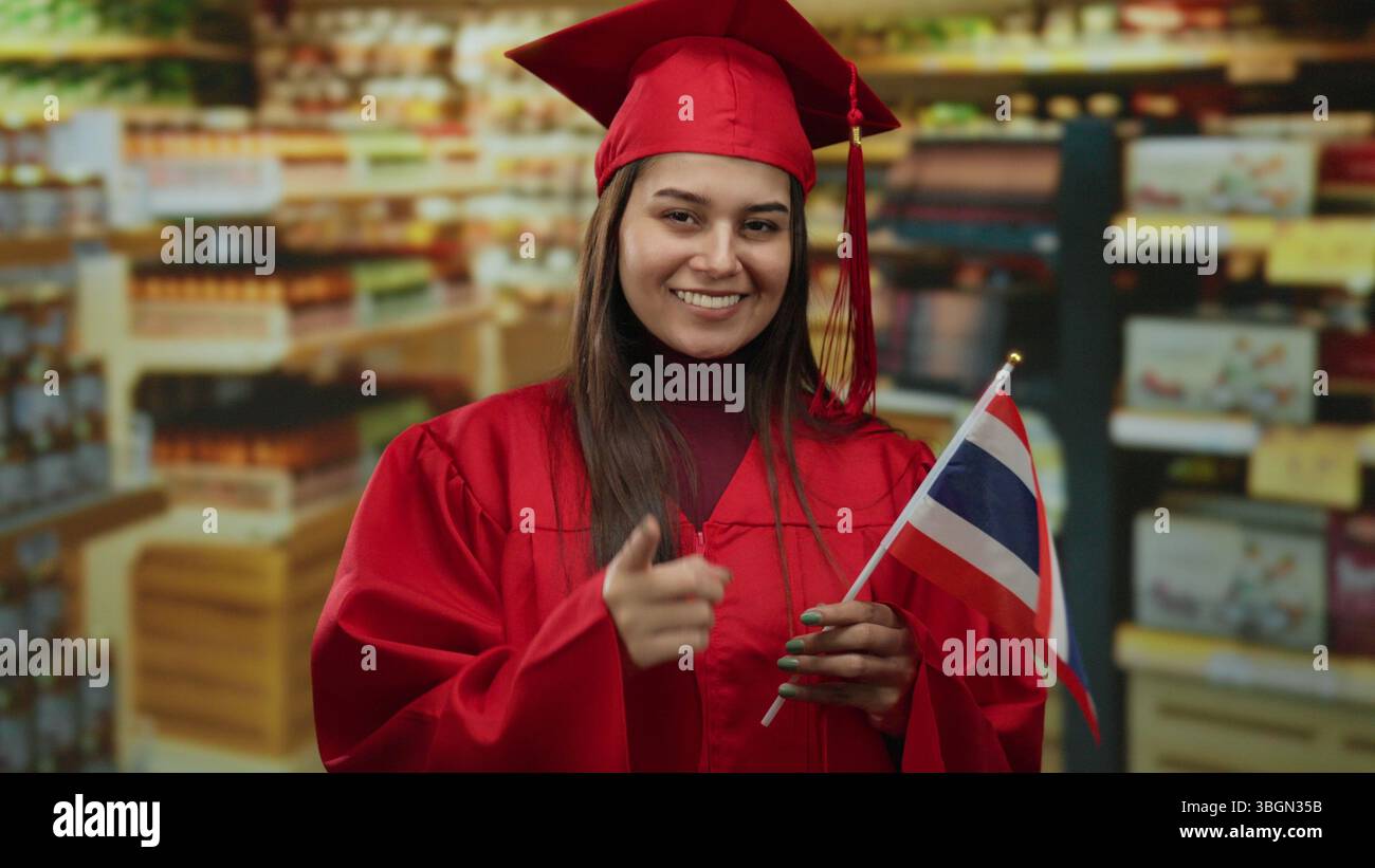 Woman in red graduation gown holds thailand flag inside a supermarket ...