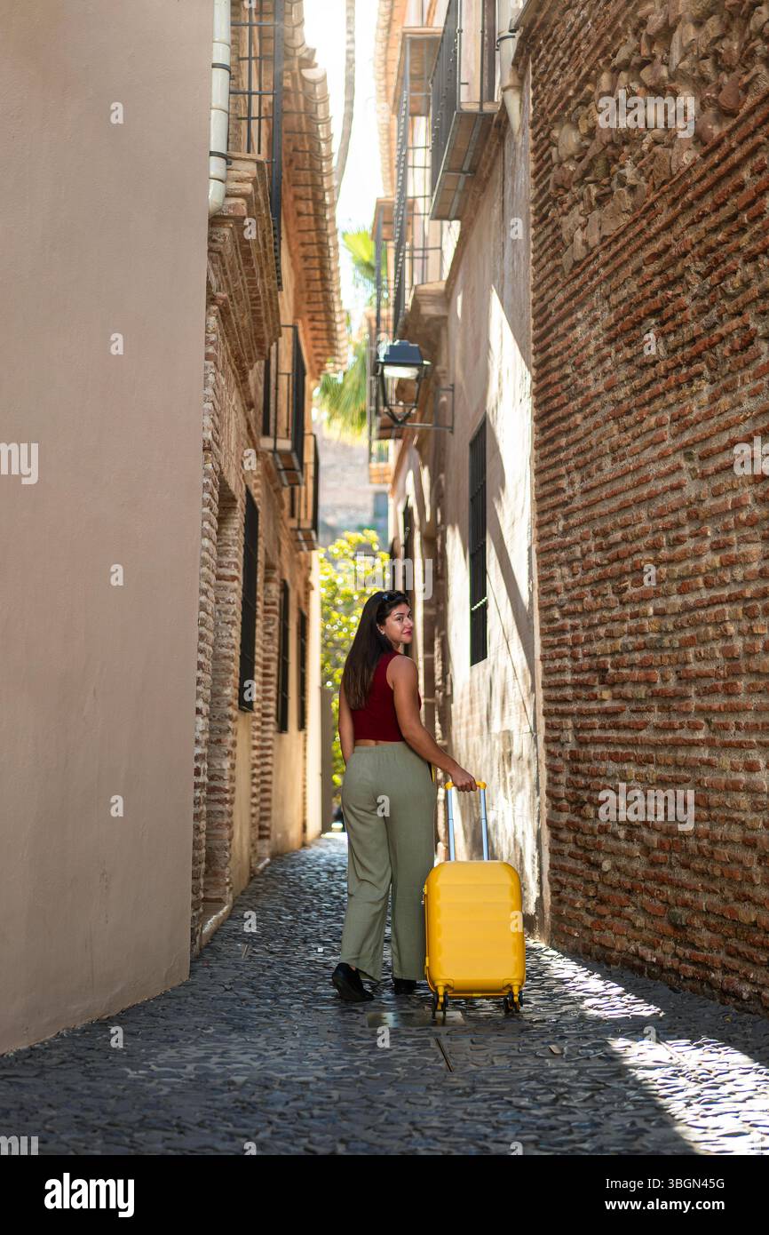Girl walks with yellow suitcase through medieval alley in downtown ...
