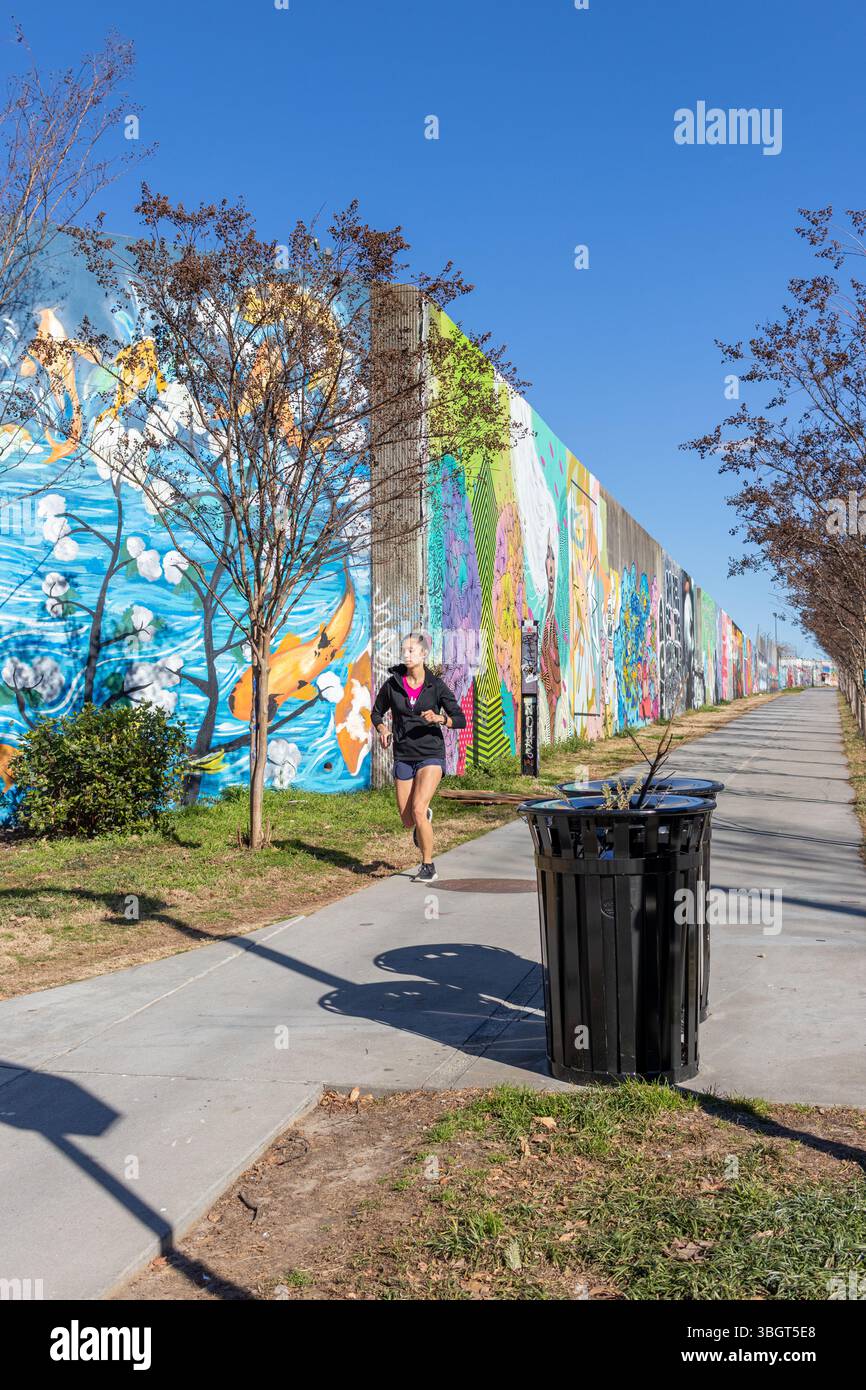 A woman is running on a sidewalk next to a wall covered in colorful ...