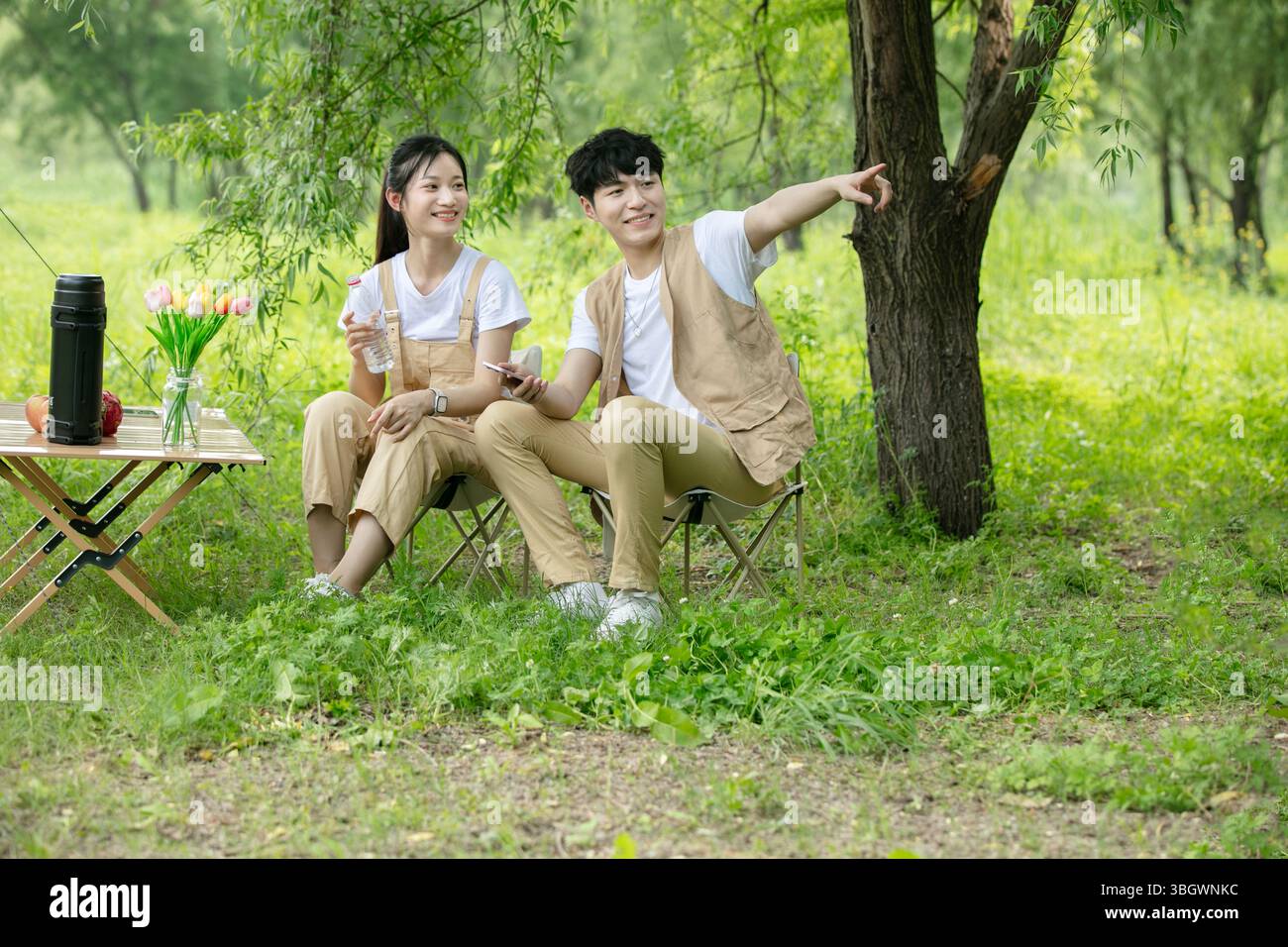 a young couple resting under a big tree while using their phones Stock ...