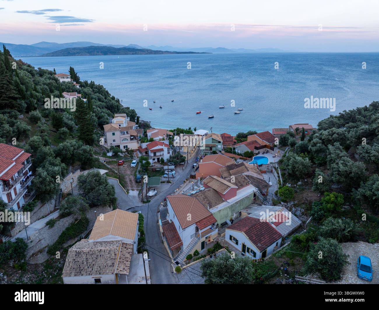 Coastal village homes dot a hillside overlooking a serene ocean under a pastel sunrise sky Stock ...
