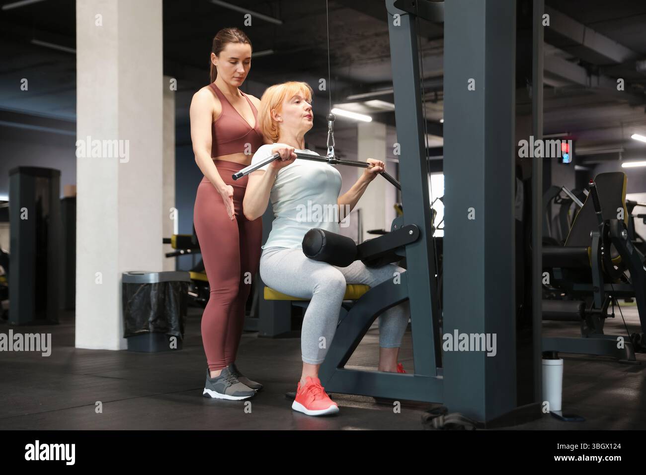 Senior woman training on lat pulldown machine supervised by ...