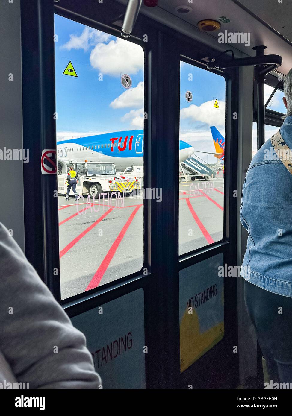 Crowded airport bus interior filled with standing passengers holding onto handrails during ...