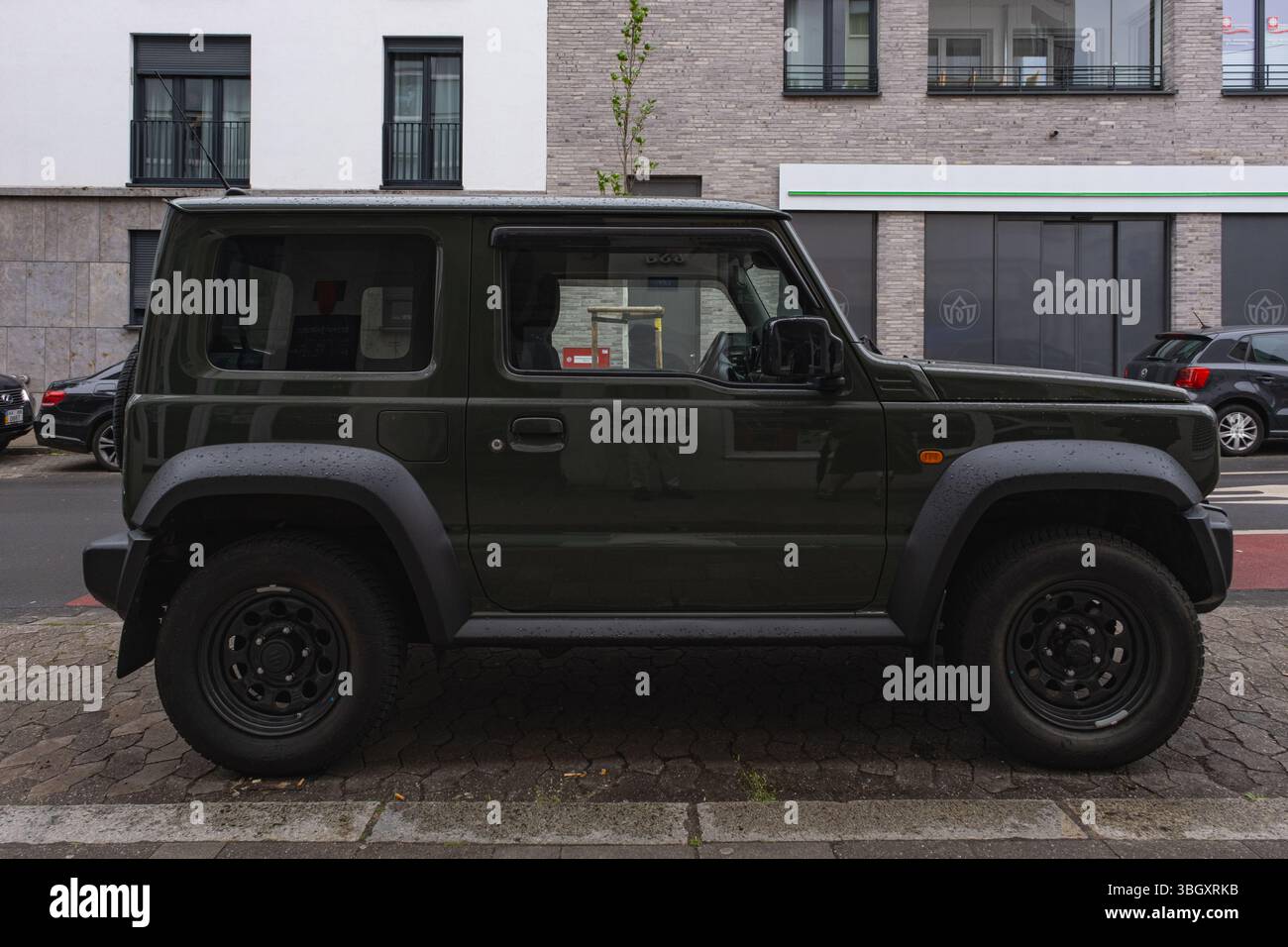 Dark green off-road SUV Suzuki Jimny parked on a quiet urban street ...