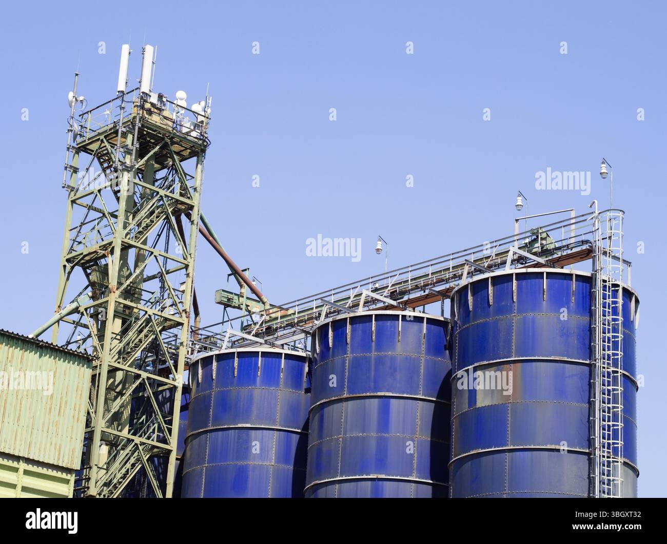 Large, blue industrial silos stand alongside a tall metal framework ...