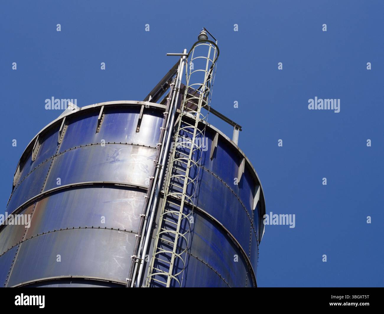 A striking low-angle view of a tall, blue industrial silo with an ...