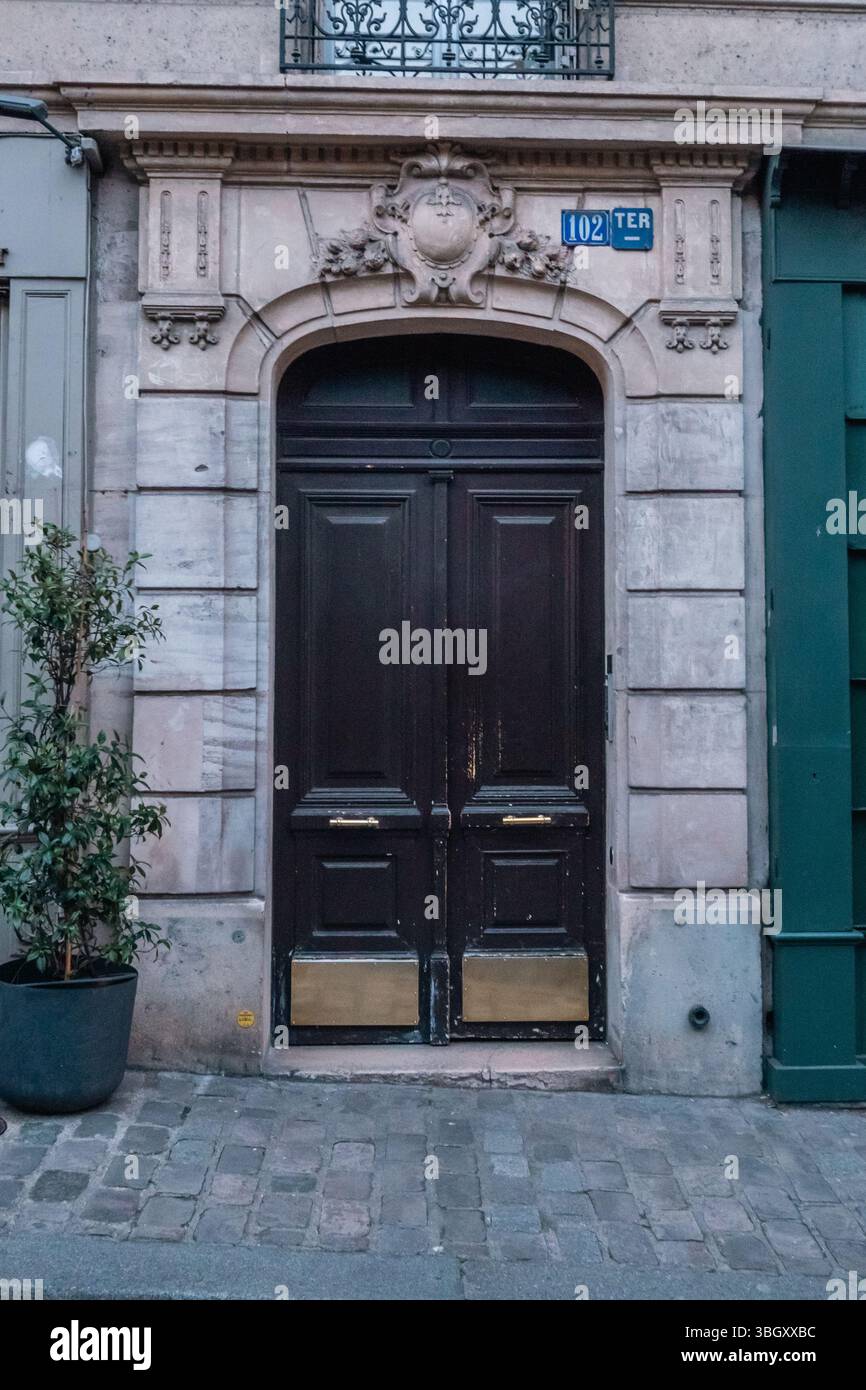 An elegant dark wooden double door is set within an ornate stone archway on a classic Parisian ...