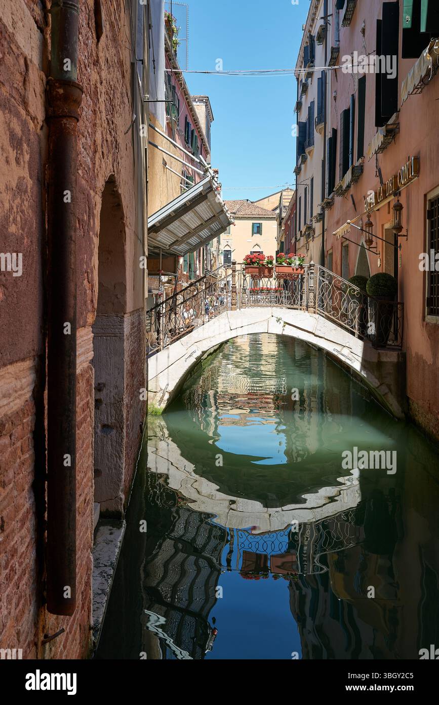 A traditional arched stone bridge spans a peaceful canal in Venice ...