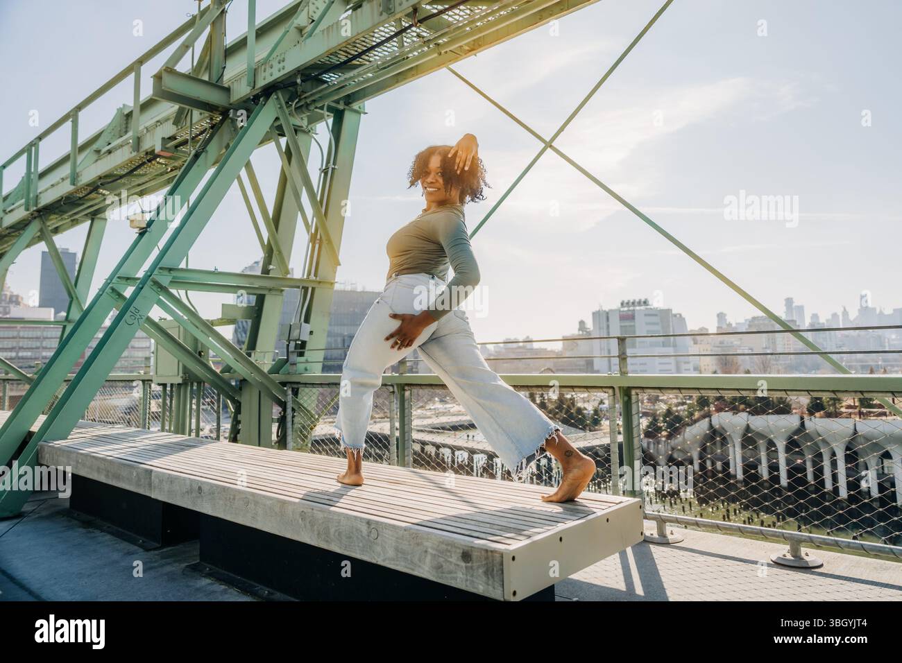 Smiling woman striking a pose on a bench with city backdrop Stock Photo ...