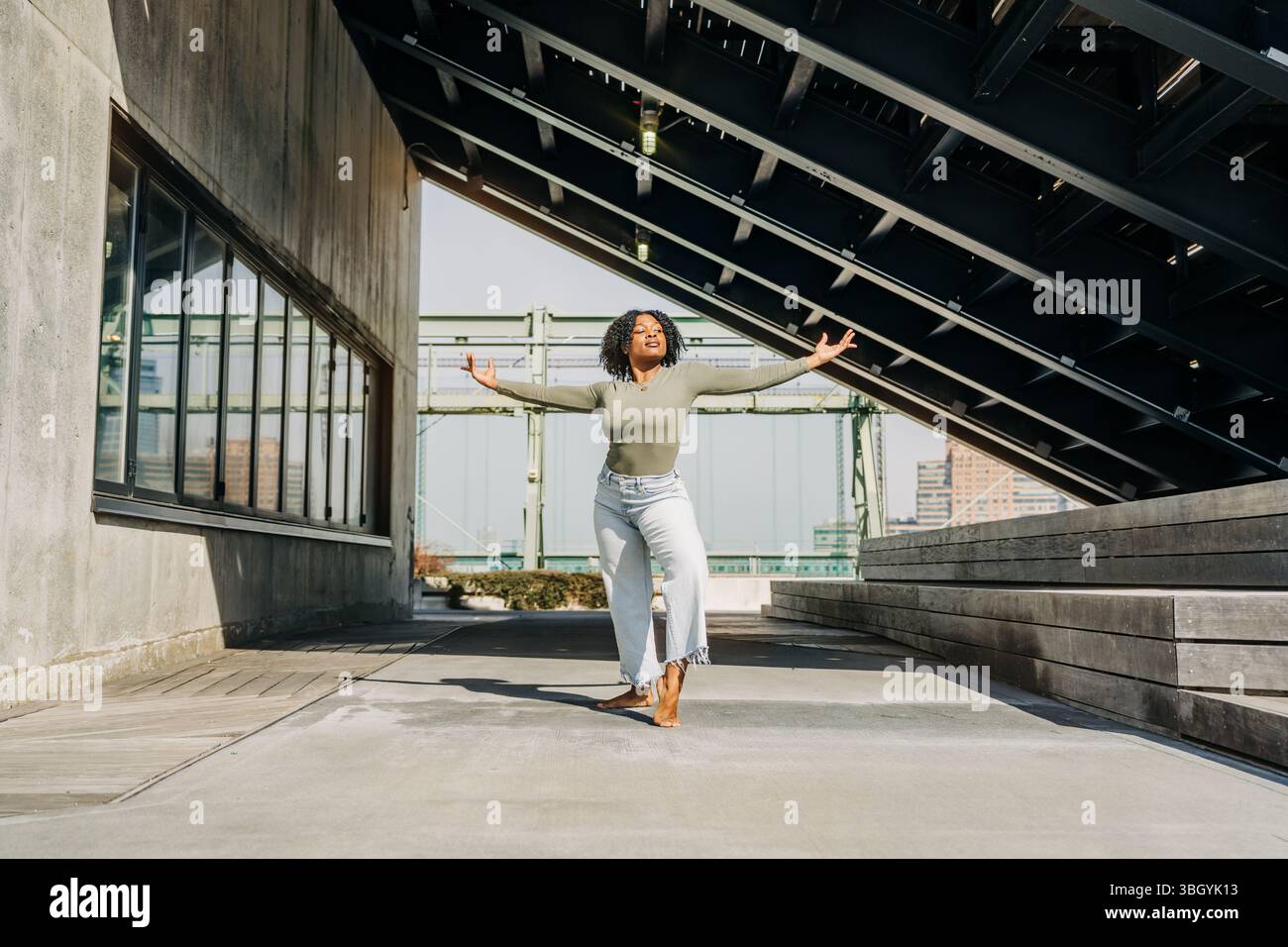 Dancer poses with arms open under industrial canopy structure Stock ...