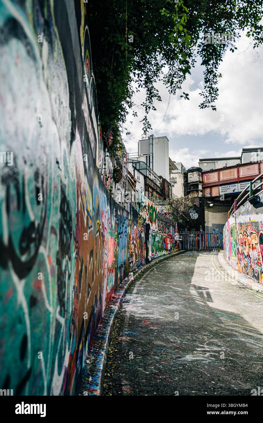 Graffiti-covered alley curves under trees in urban setting Stock Photo ...