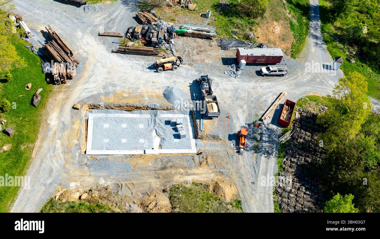 A construction site shows a freshly laid concrete foundation surrounded ...