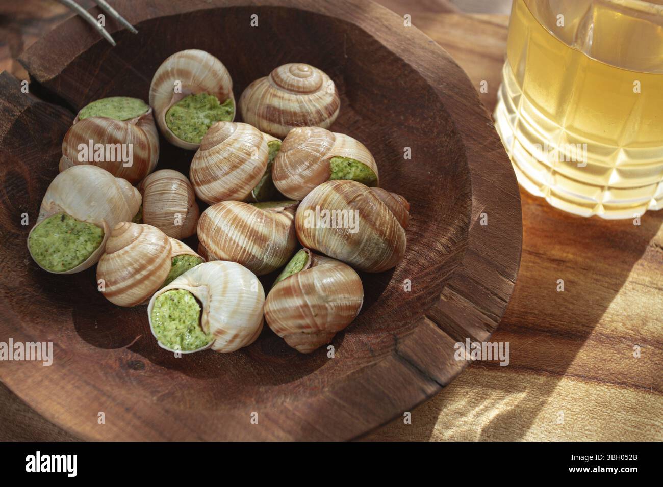 Snails cooked with herb oil on a wooden plate, served with white wine ...