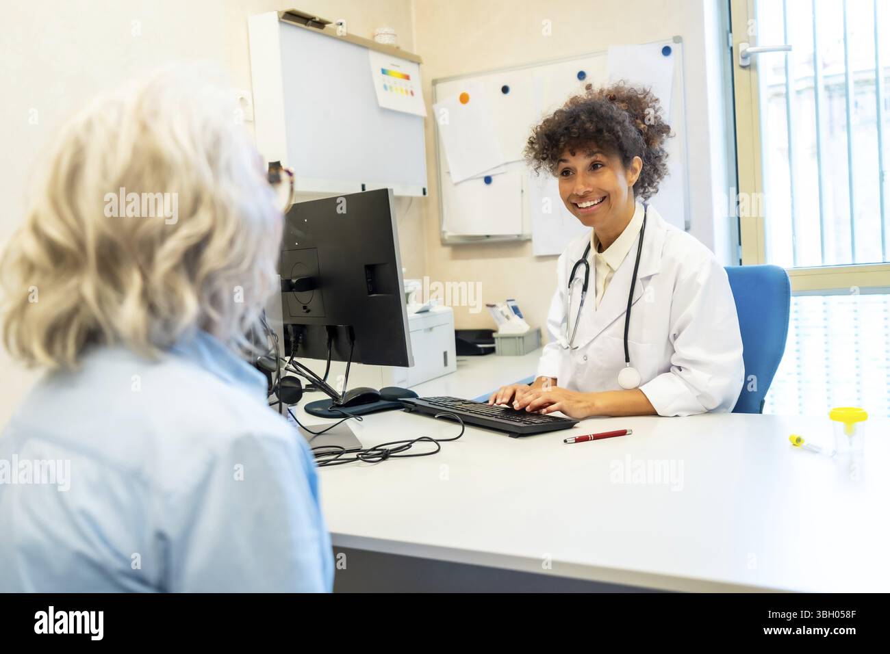 Smiling female doctor wearing lab coat and stethoscope typing on ...