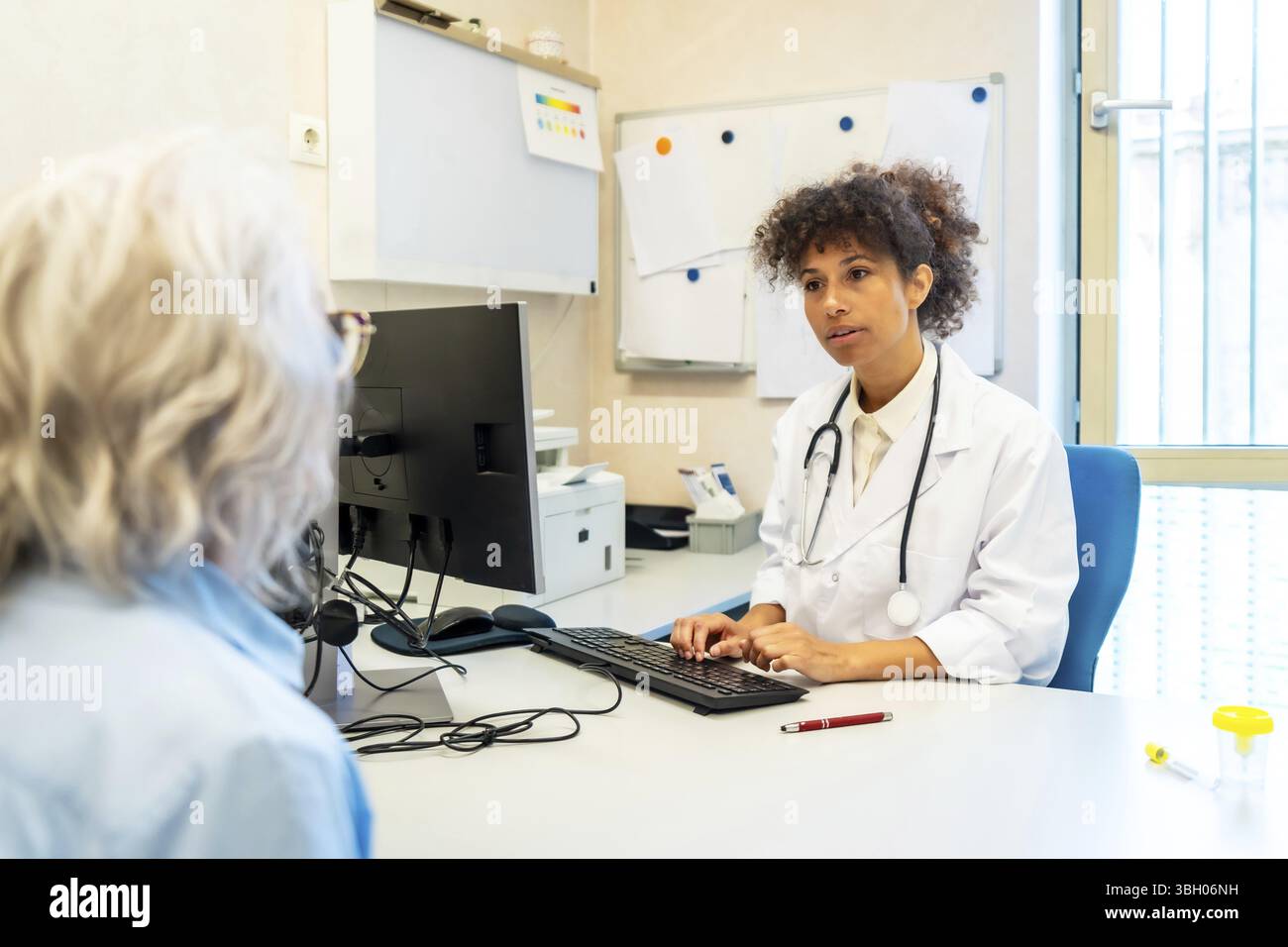Female doctor using computer and listening to senior patient describing ...