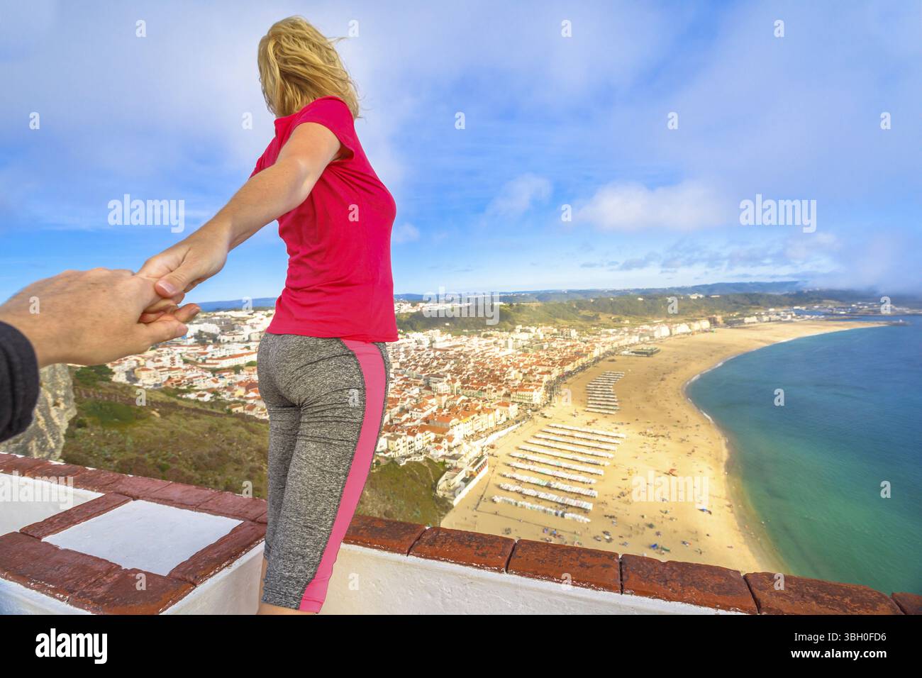 Follow me, blonde caucasian woman holding man hand with Nazare skyline ...