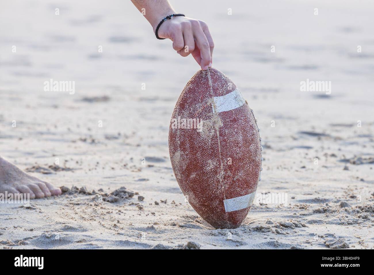 Close up of hand over from rugby ball on sand. Hand of football player ...