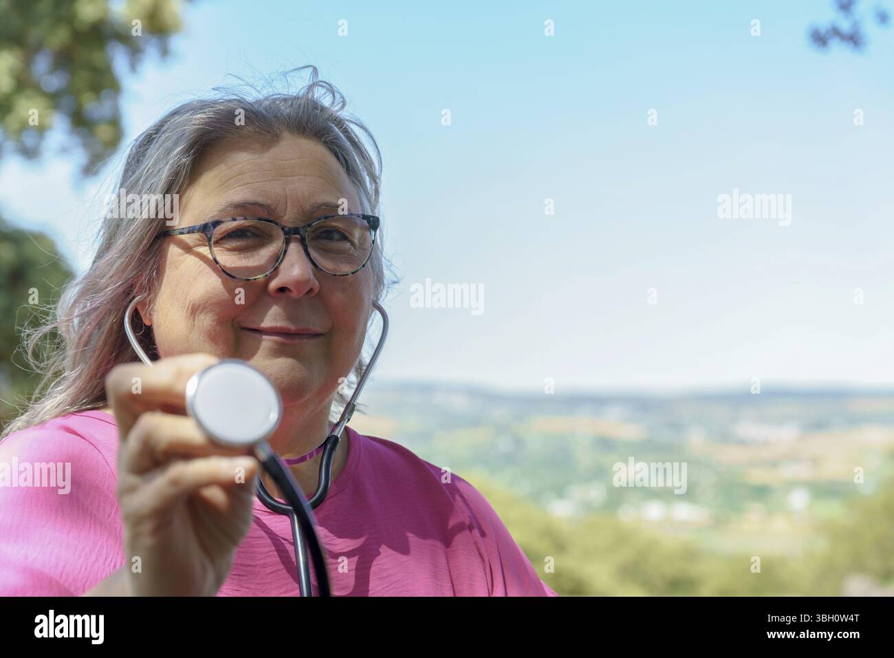 Mature female doctor holding stethoscope in nature promoting healthcare ...