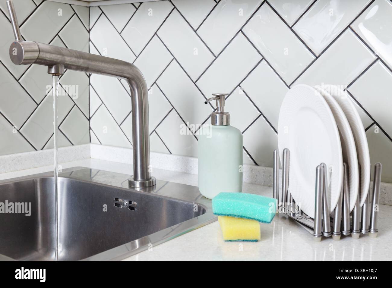 Running water from kitchen sink beside soap dispenser, stacked white ...