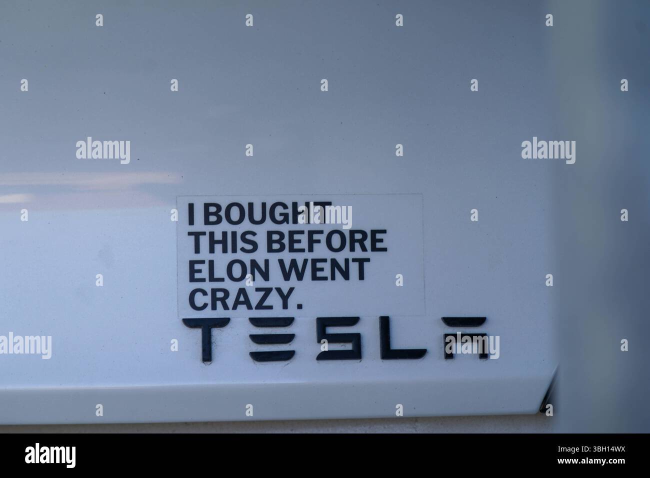 Auf dem Heck eines weißen Tesla-Fahrzeugs ist ein auffälliger Sticker ...