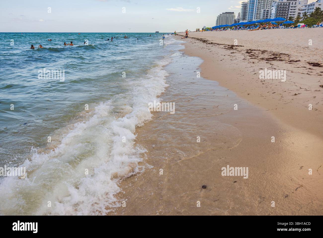Waves washing over wet sand with people swimming and sunbathing on ...