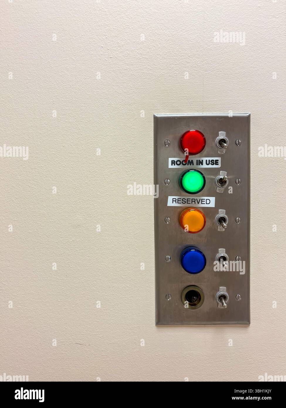 A wall-mounted metal panel features five colored lights with toggle ...