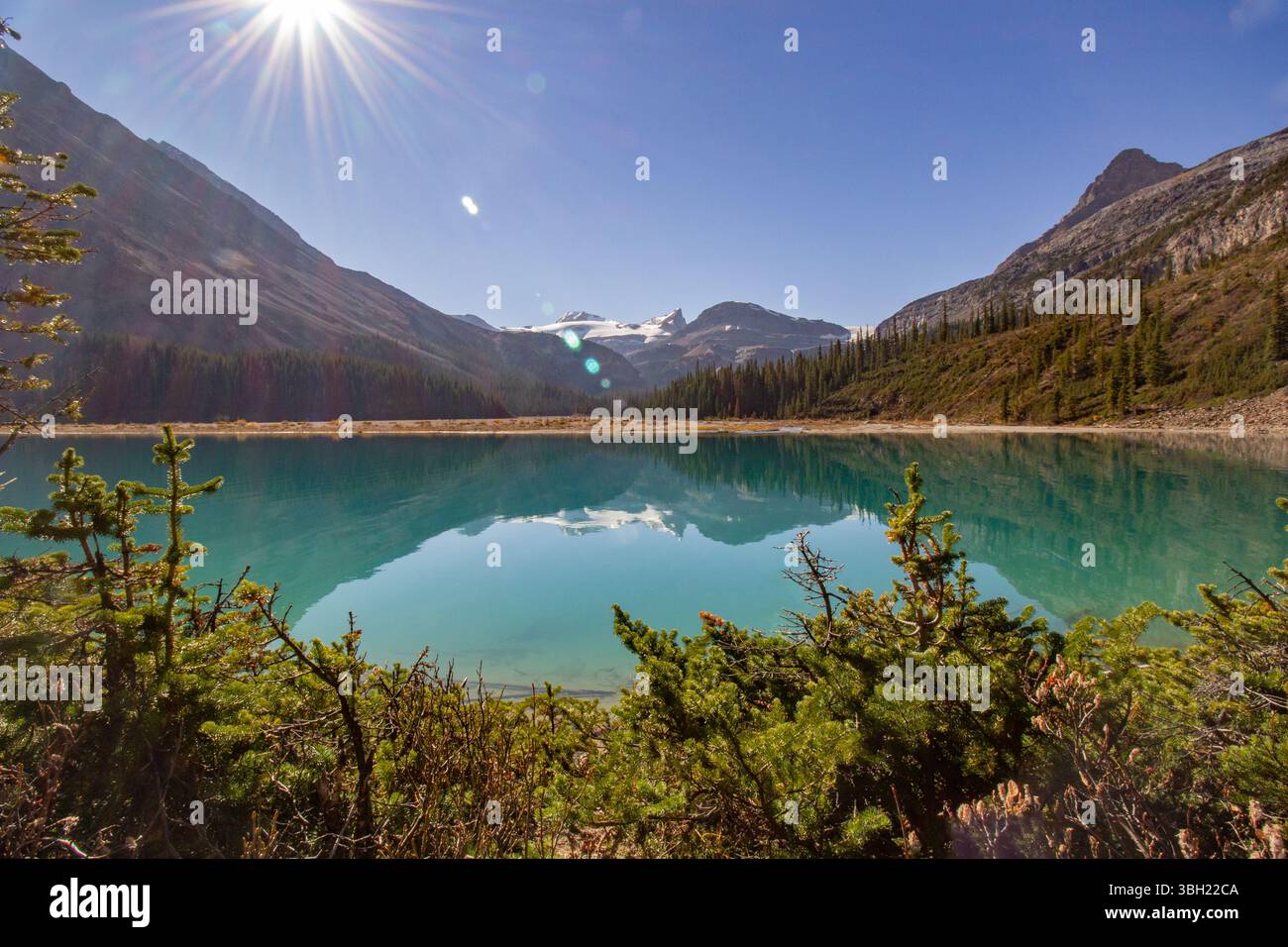 A view of a glass-like teal coloured lake glistening with sun rays and ...