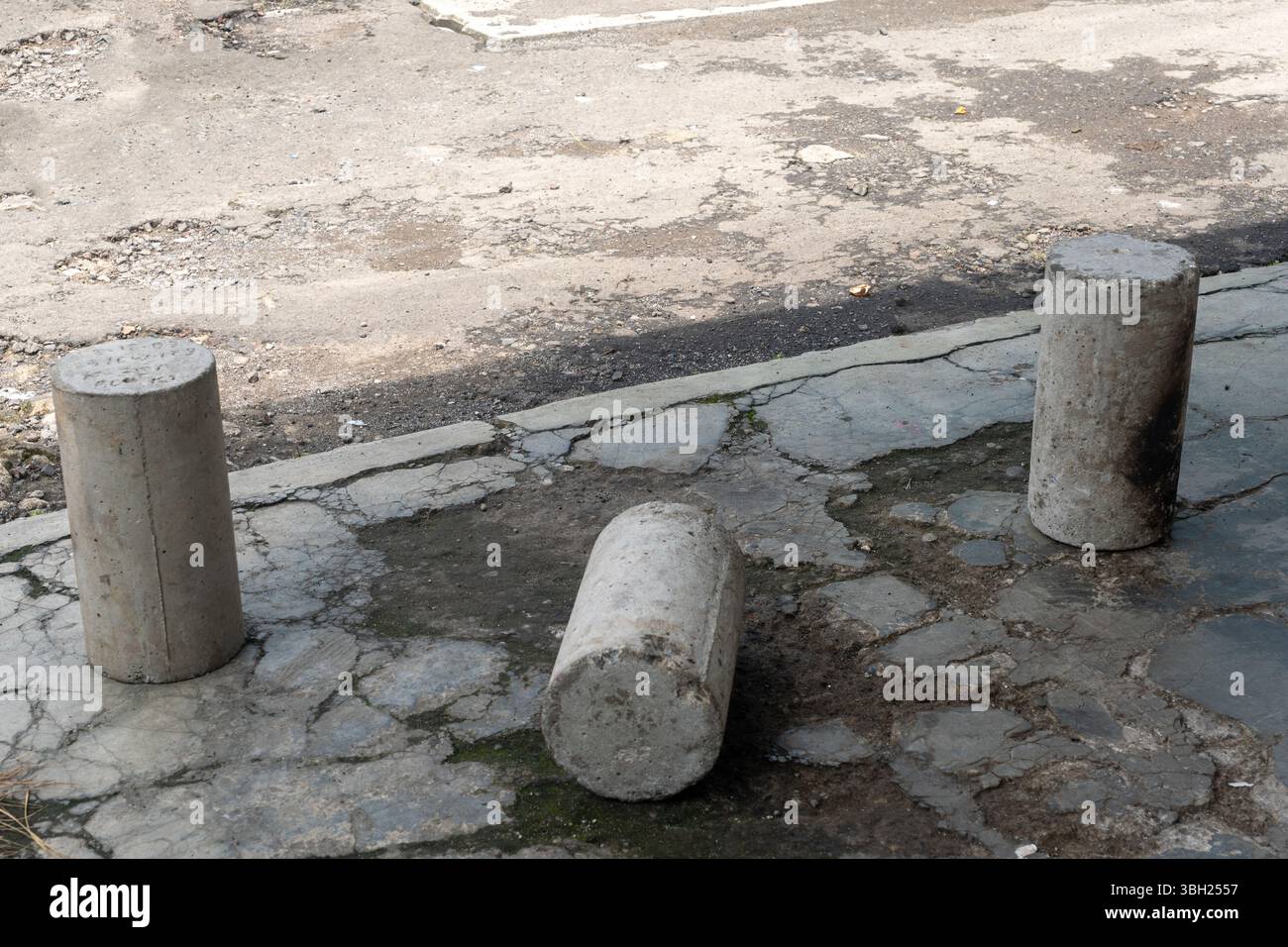 Three cement pillars are laying on the ground in front of a road. The ...