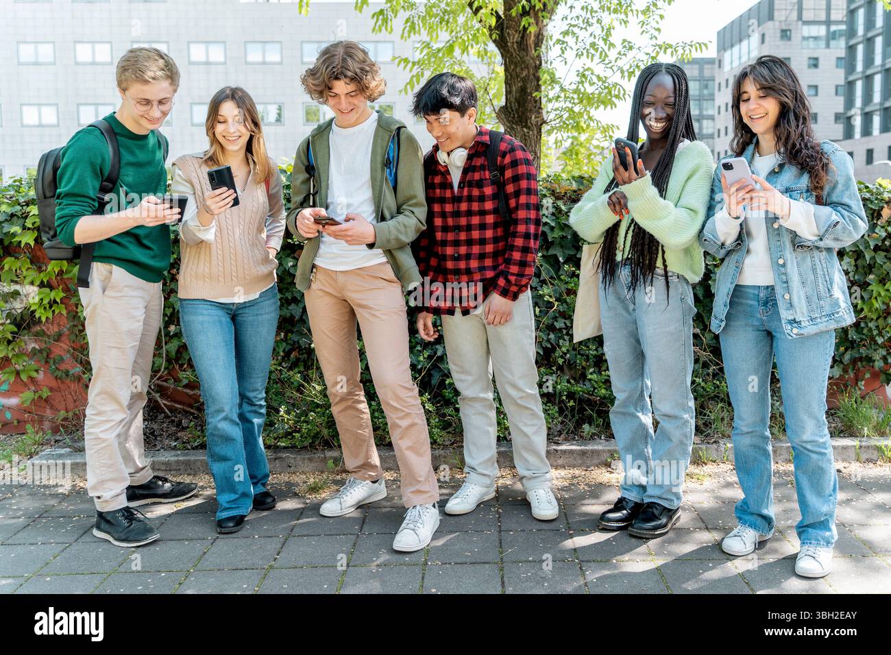 Multicultural group of teenage students standing outdoors using ...