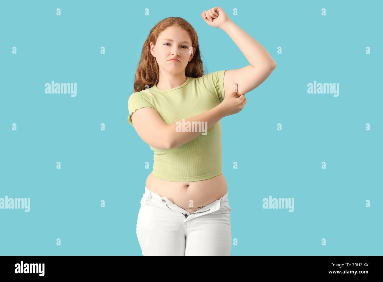 Sad young woman in tight jeans with chubby arms on blue background ...