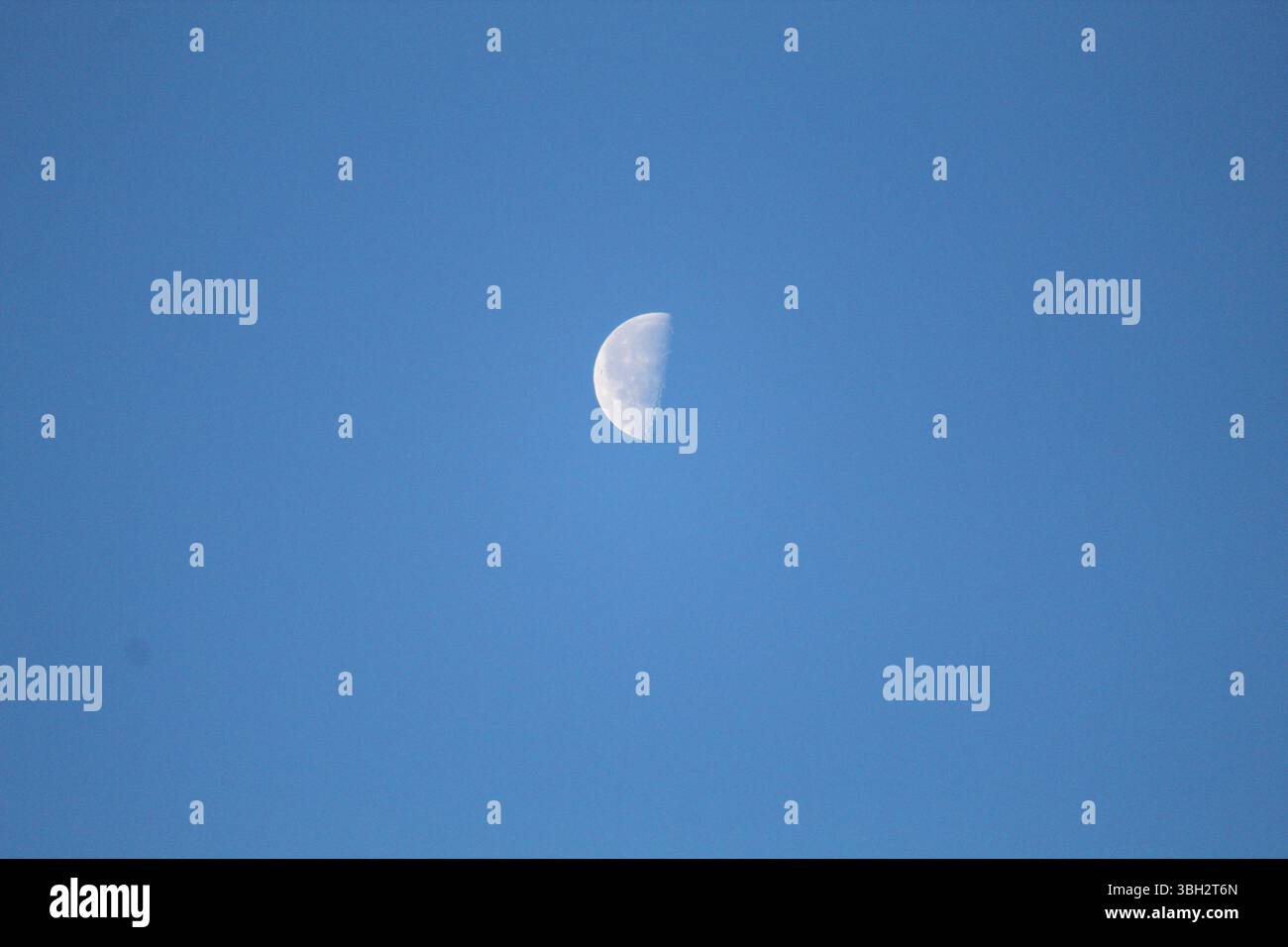 Half moon against a clear blue sky, showcasing detailed lunar surface ...