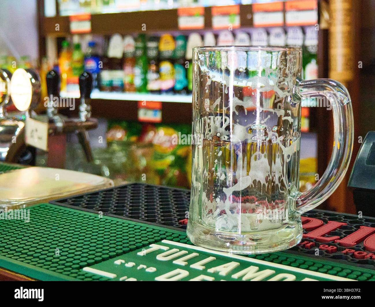 Empty, foamy beer mug on a bar counter in a pub, with blurred bottles ...