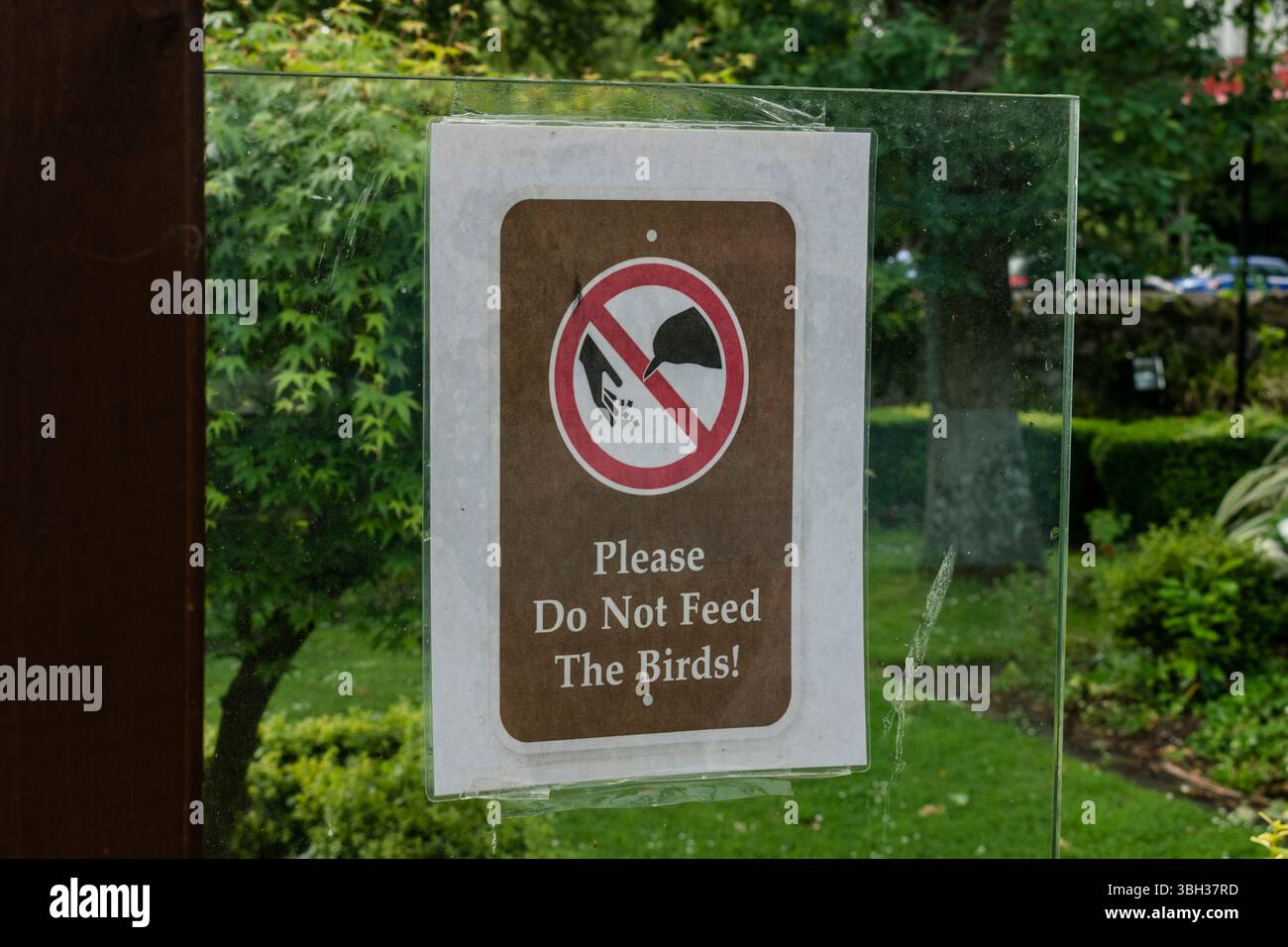 Sign on Glass Saying "Please Do Not Feed the Birds" with park view ...