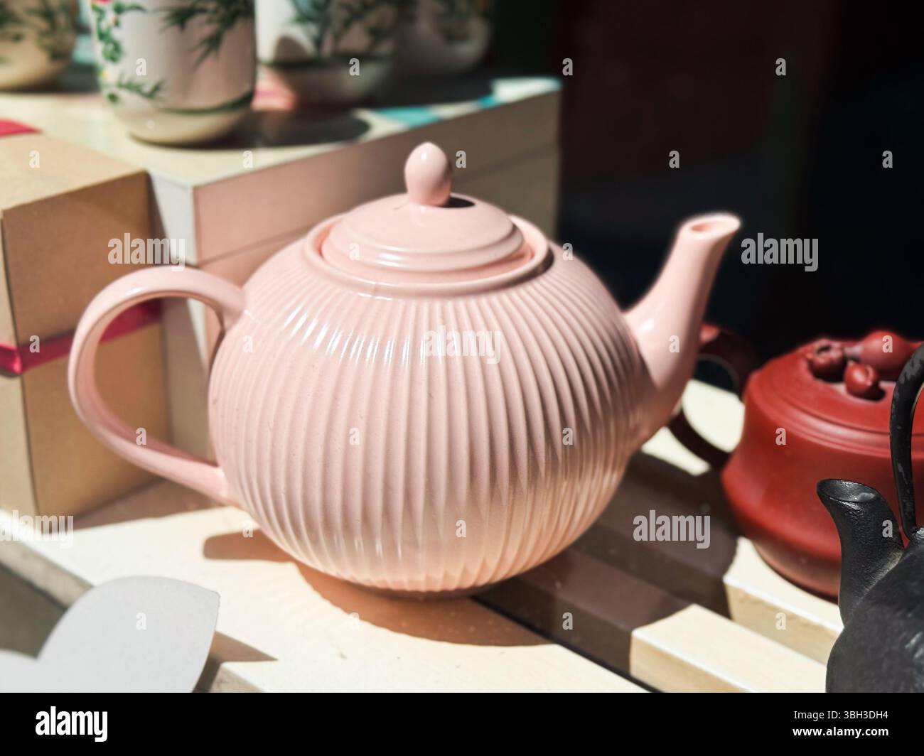 Pink ceramic teapot in sunlight. Ribbed teapot on display with other ...