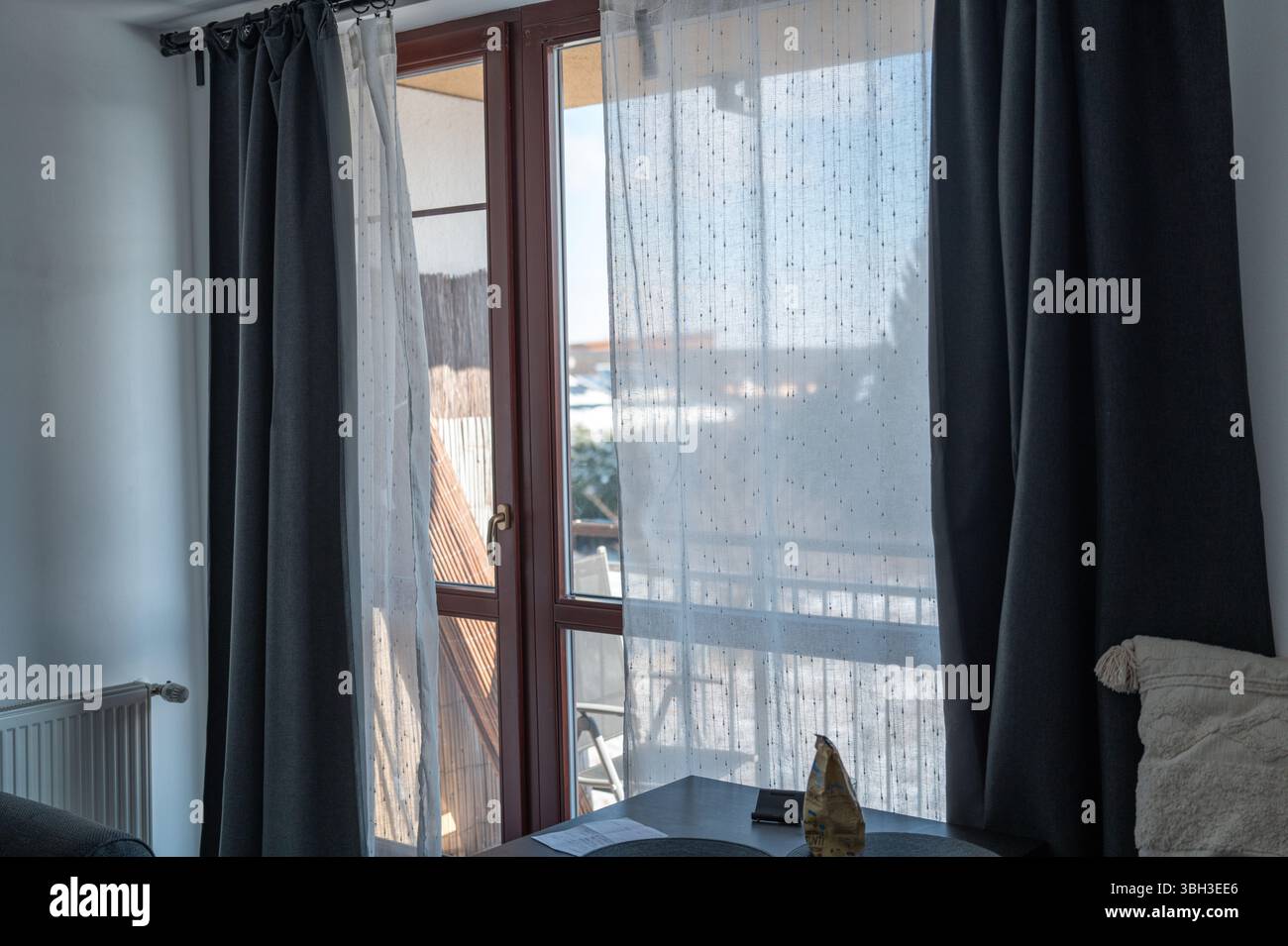 Bright interior view through sheer and dark curtains to a balcony with ...