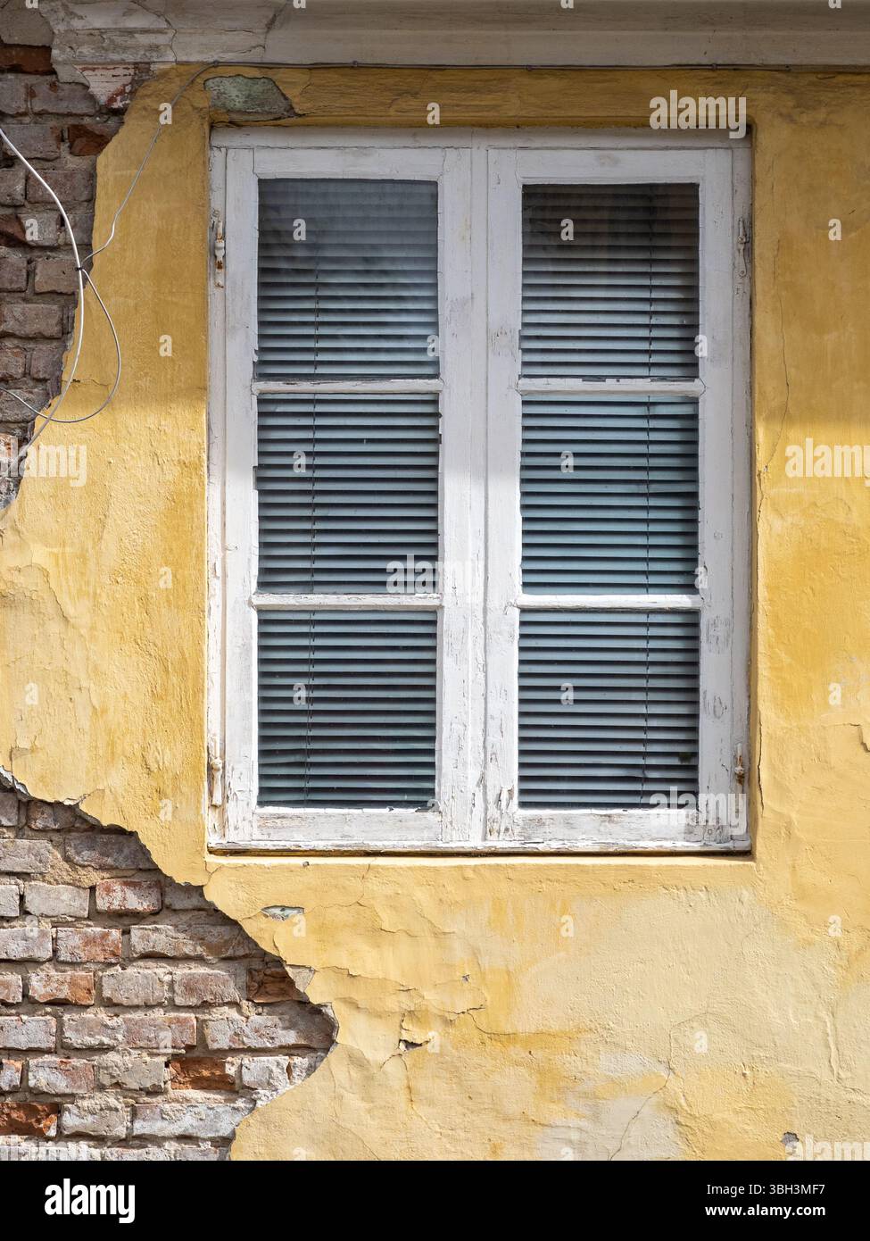 Wood-framed window with shades in a derelict yellow building with ...