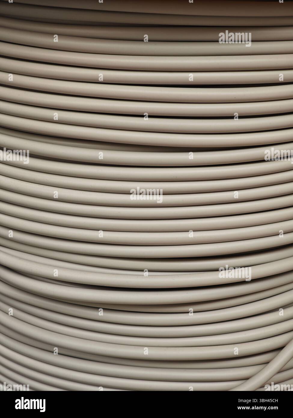 Multiple rolls of beige electrical cables are arranged in a neat stack ...