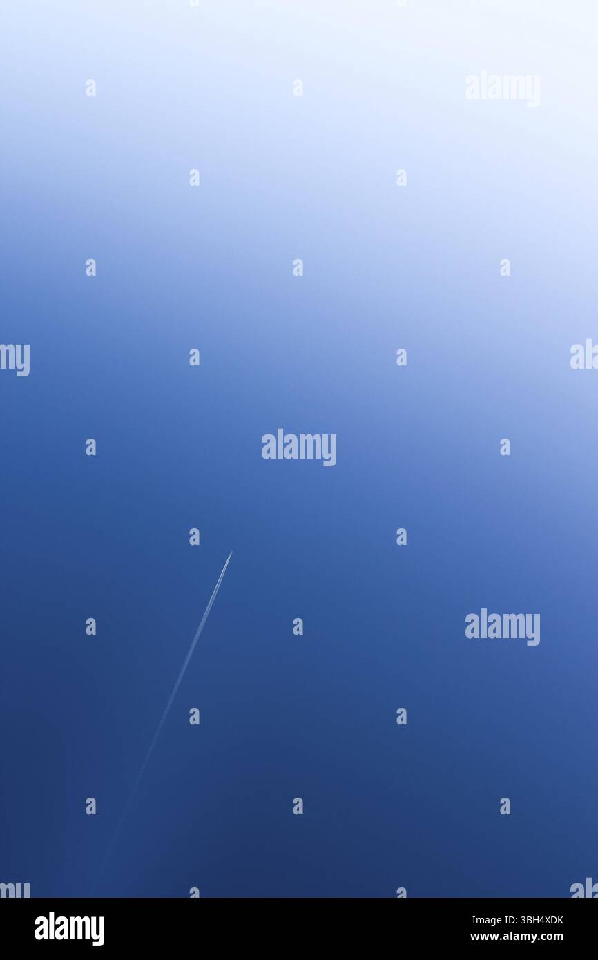 Airplane flying at high altitude leaving its white wake over blue sky ...