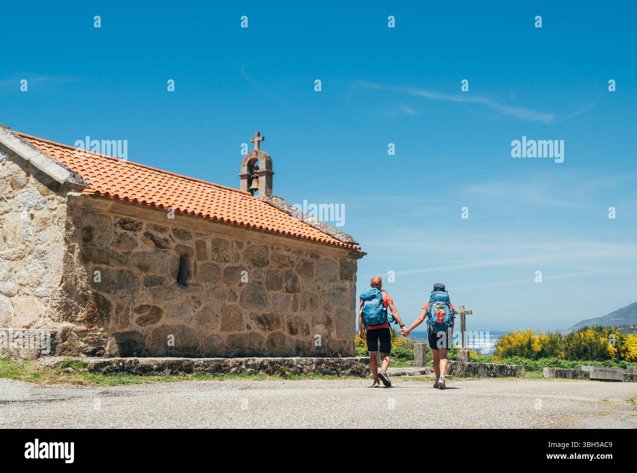 Couple of pilgrims with backpacks walking hand in hand next to old ...