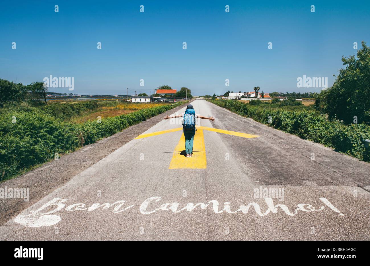Joyful female pilgrim with backpack walking on yellow arrow road ...