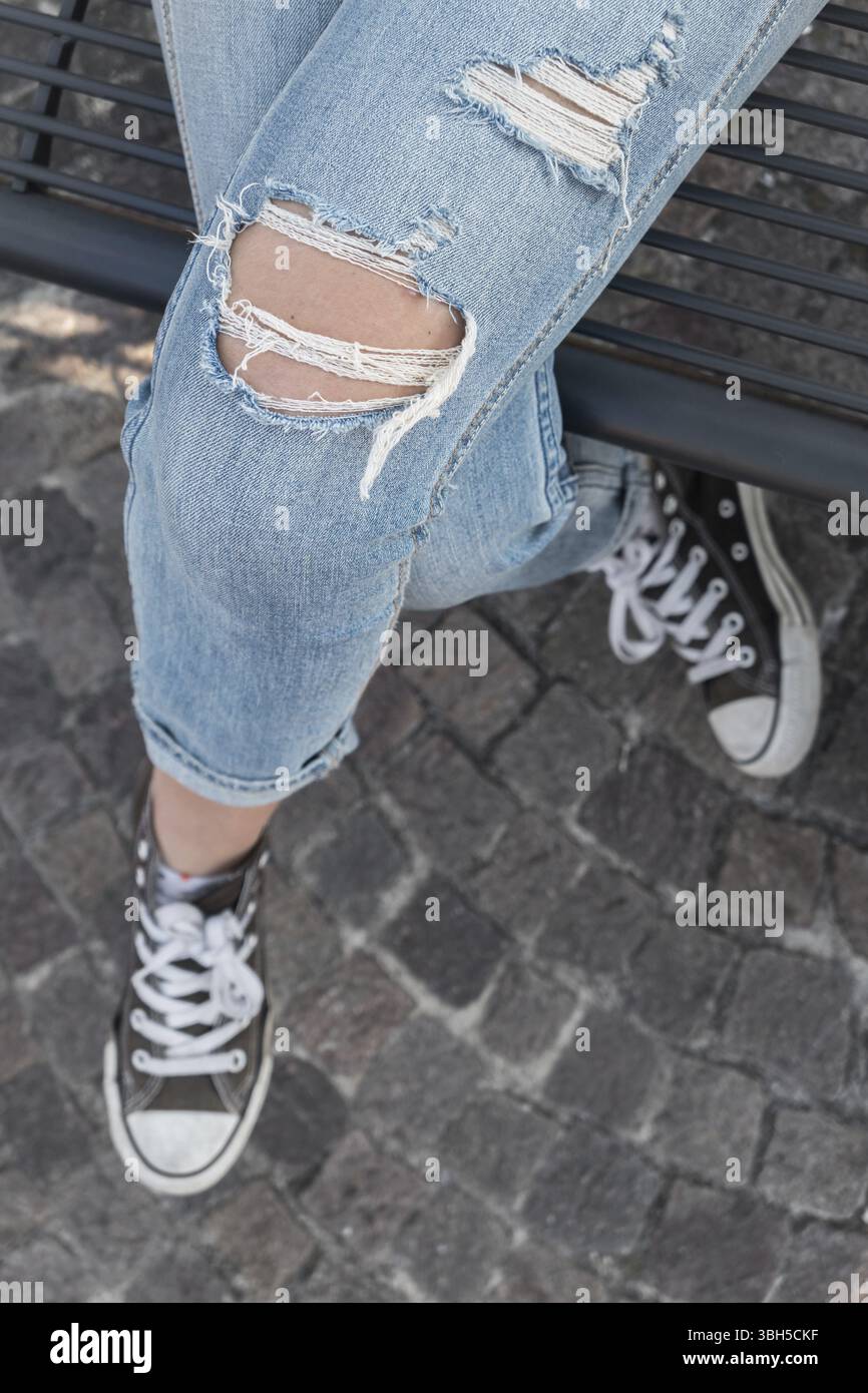Woman wears trendy torn jeans and black shoes, she's sitting to legs ...