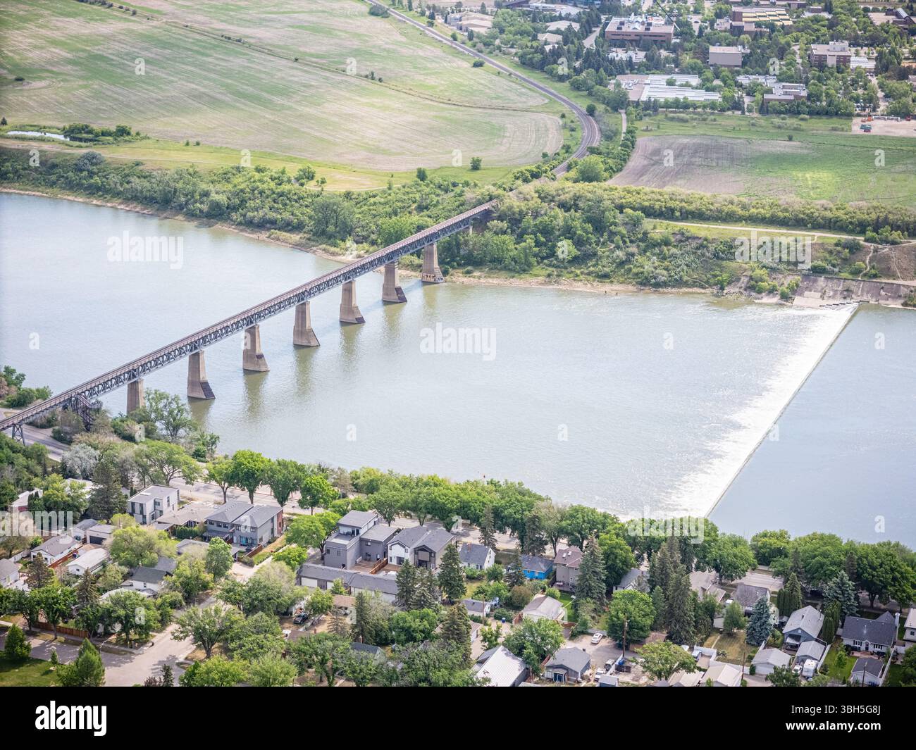 Bridge spans a river, with houses and trees in the background. The ...