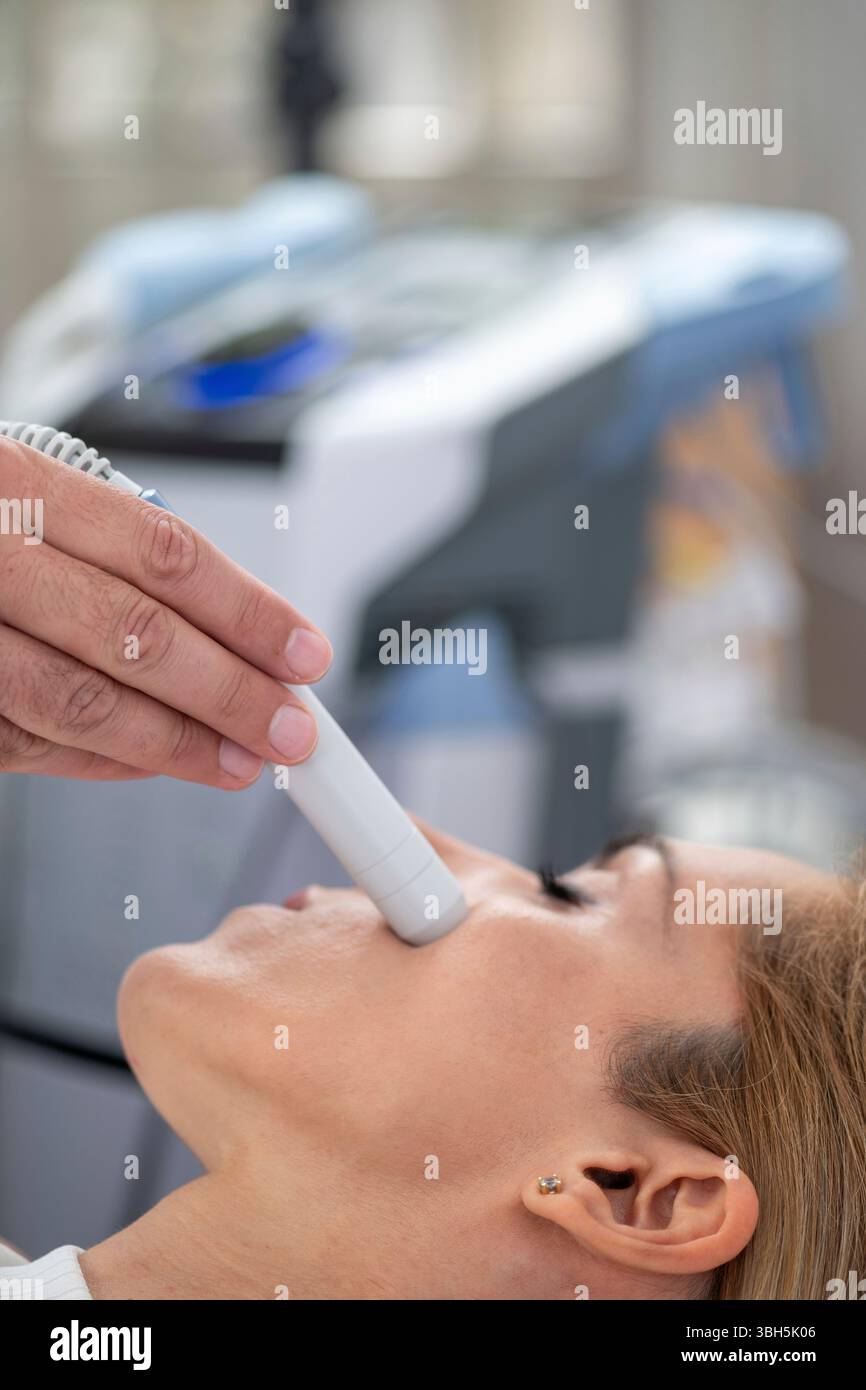 Physical therapist uses a laser to treat a patients sinus area ...