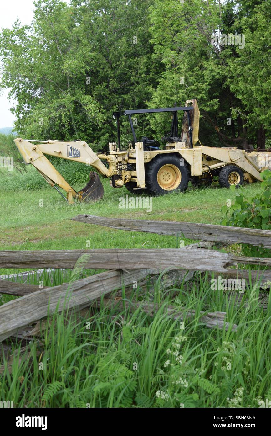 An excavator parked quietly in a grassy field surrounded by trees ...