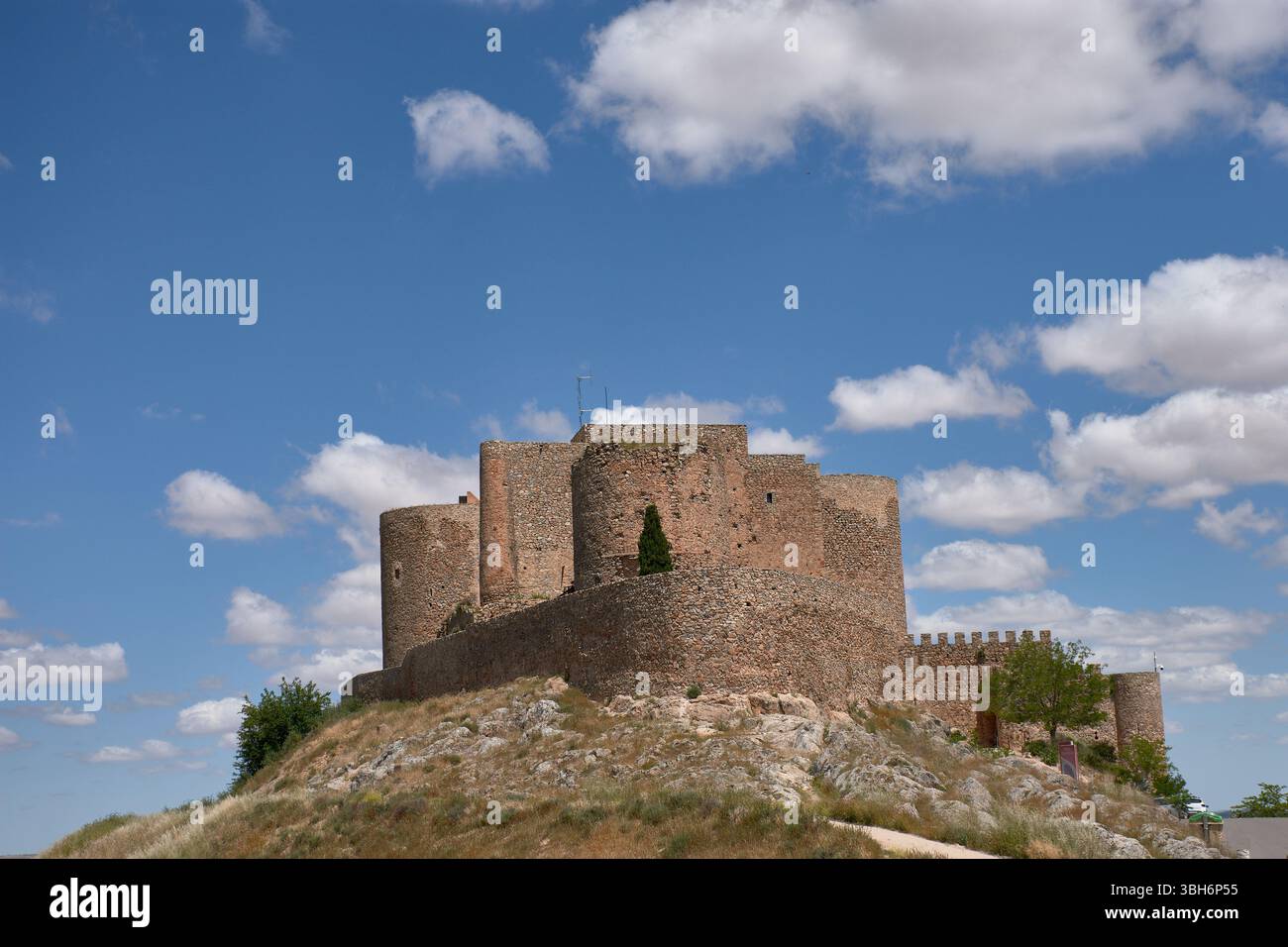 An imposing medieval castle crowns a dry, grassy hill under a bright ...