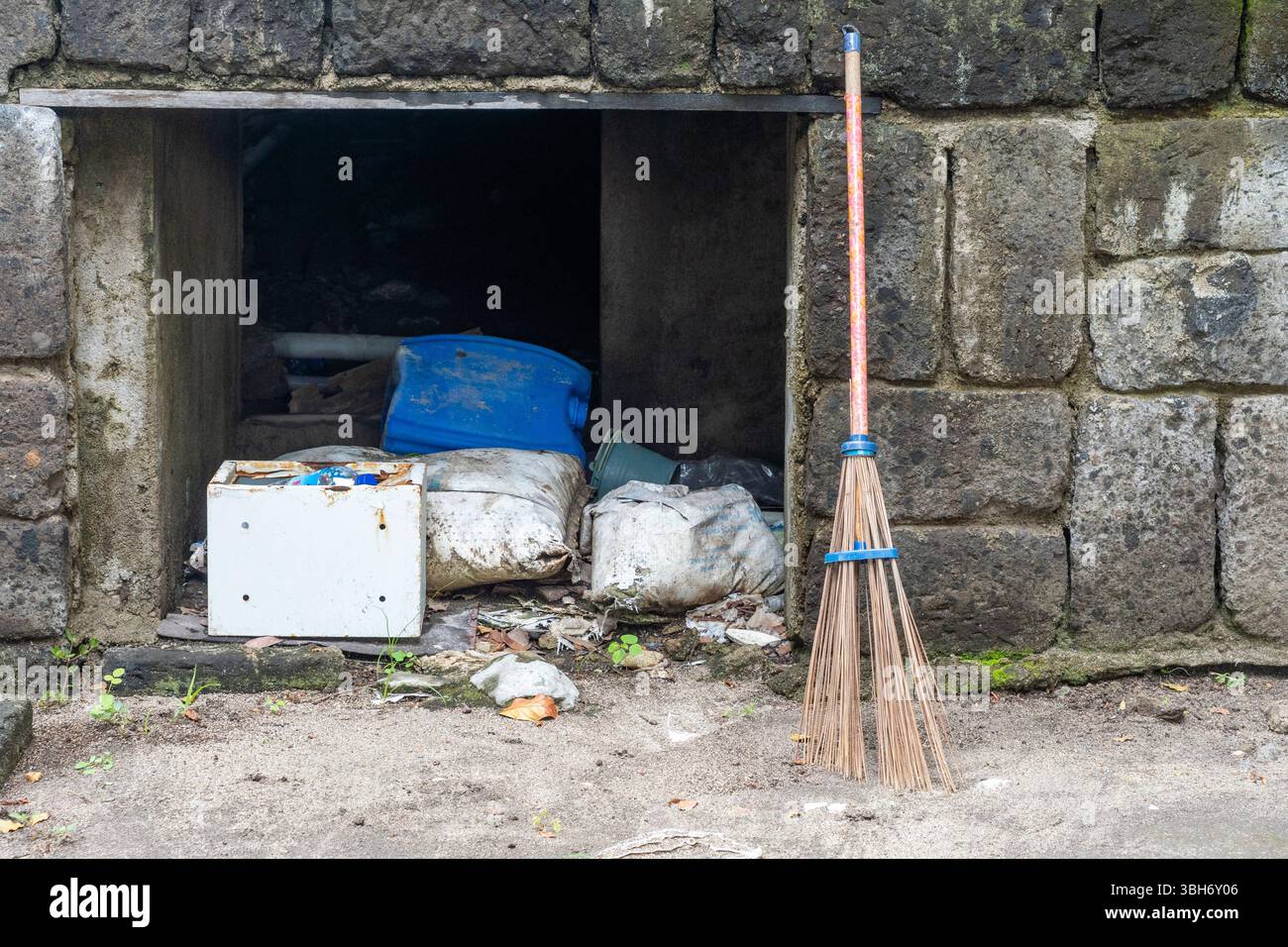 Broom is leaning against a wall next to a pile of trash. The scene is ...
